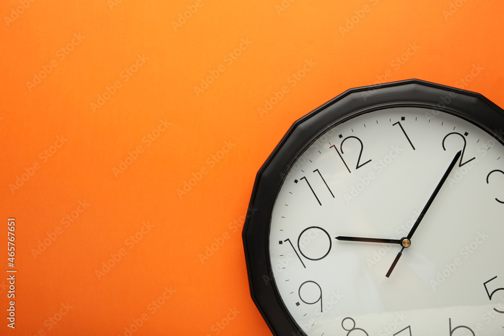 Black wall clock on the orange background. Stock Photo | Adobe Stock