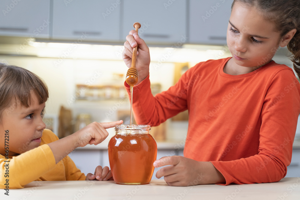 Happy children eating honey from a jar at home in the kitchen. funny ...
