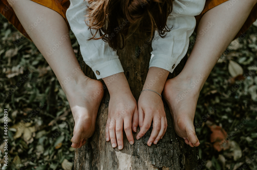 Details of woman seated on fallen tree with bare feet and hands on tree ...