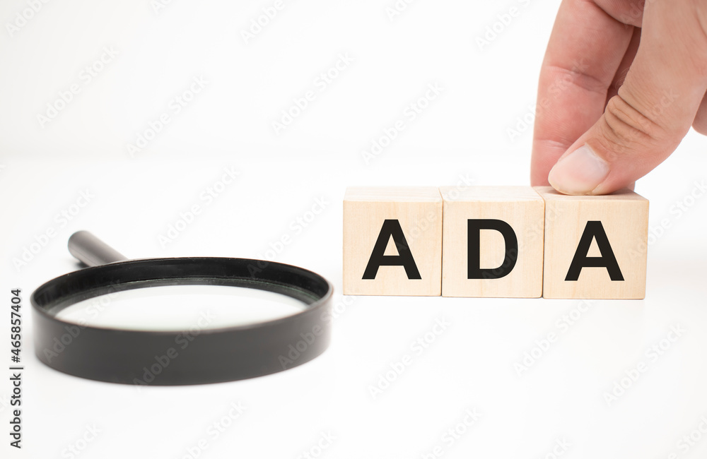 ada text wooden cube blocks and hand holding magnifying glass on table ...