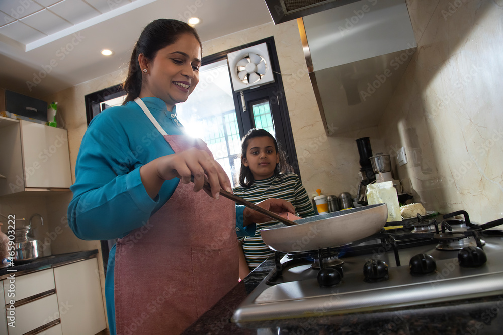 Middle class Indian woman cooking food and her daughter standing beside ...