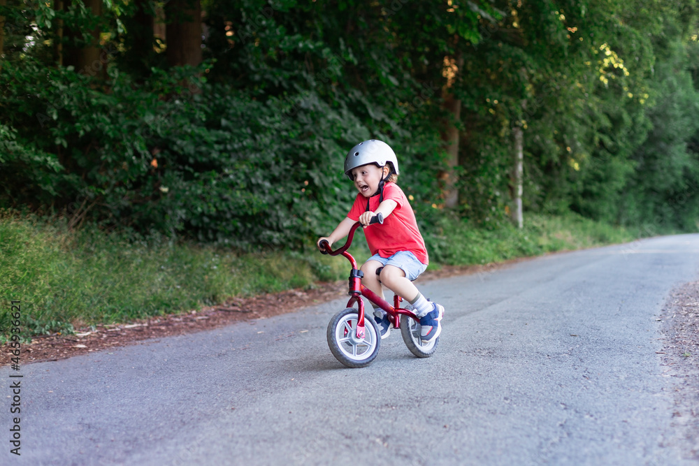 Little toddler boy wearing safety helmet is training to ride a balance bike. .Child screams with ...