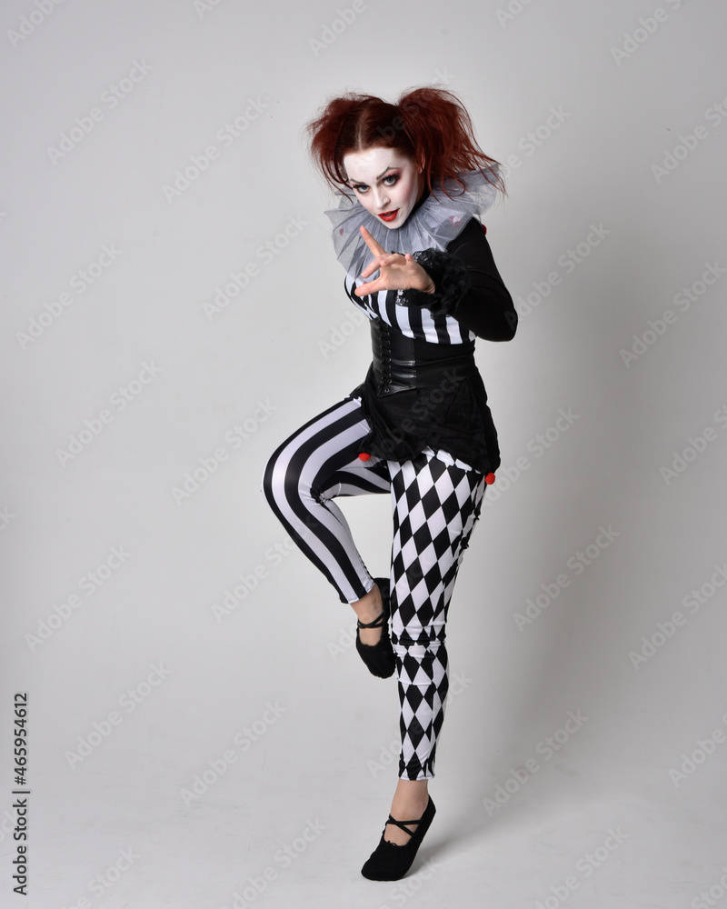 Full length portrait of red haired girl wearing a black and white clown ...