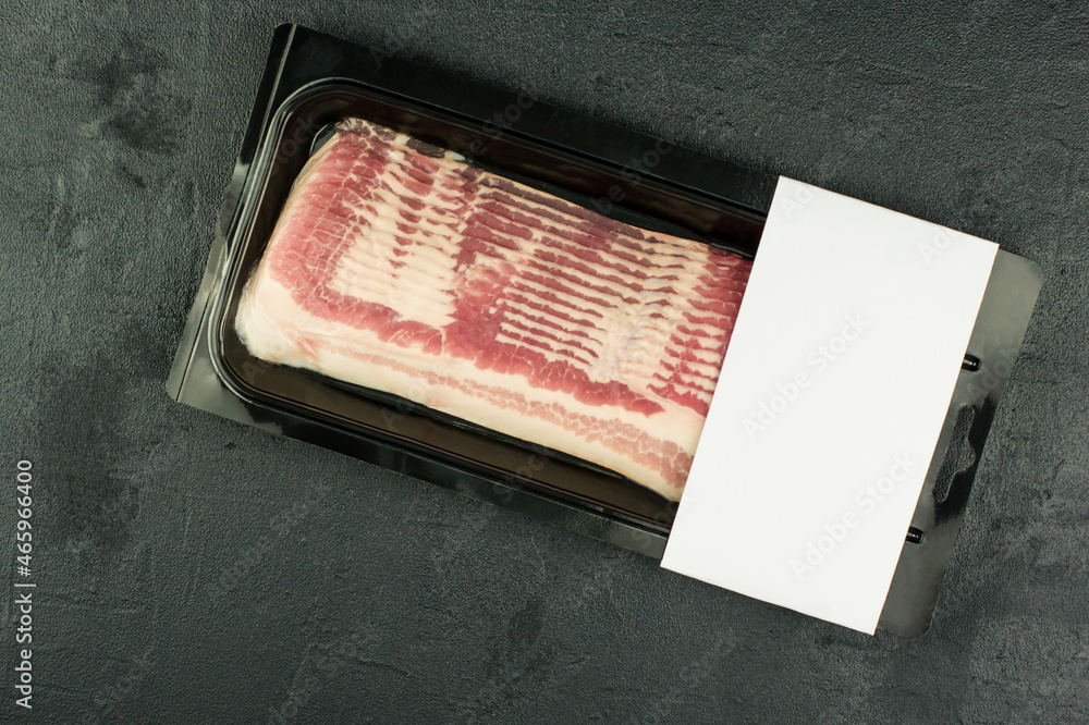 smoked pork bacon in factory plastic packaging on a black background ...