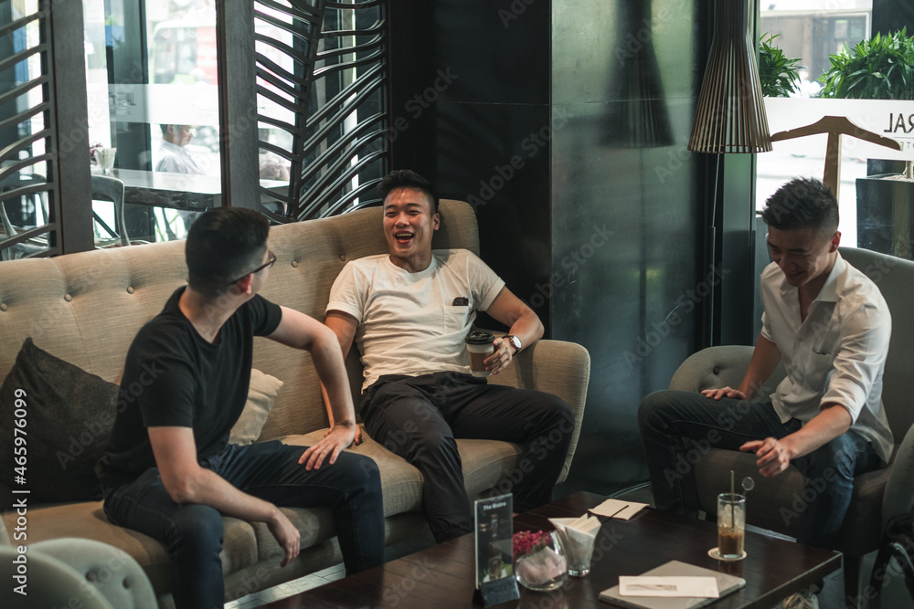 Foto de Three asian young men sitting in coffee shop, drinking coffee ...