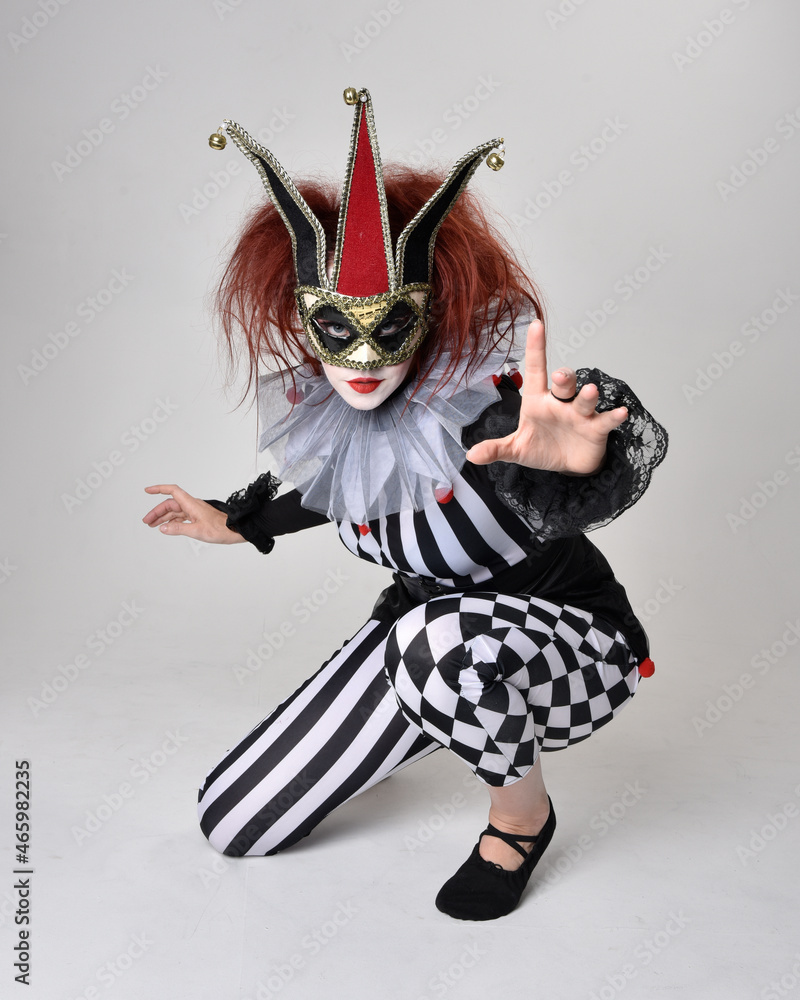 Full length portrait of red haired girl wearing a black and white clown ...