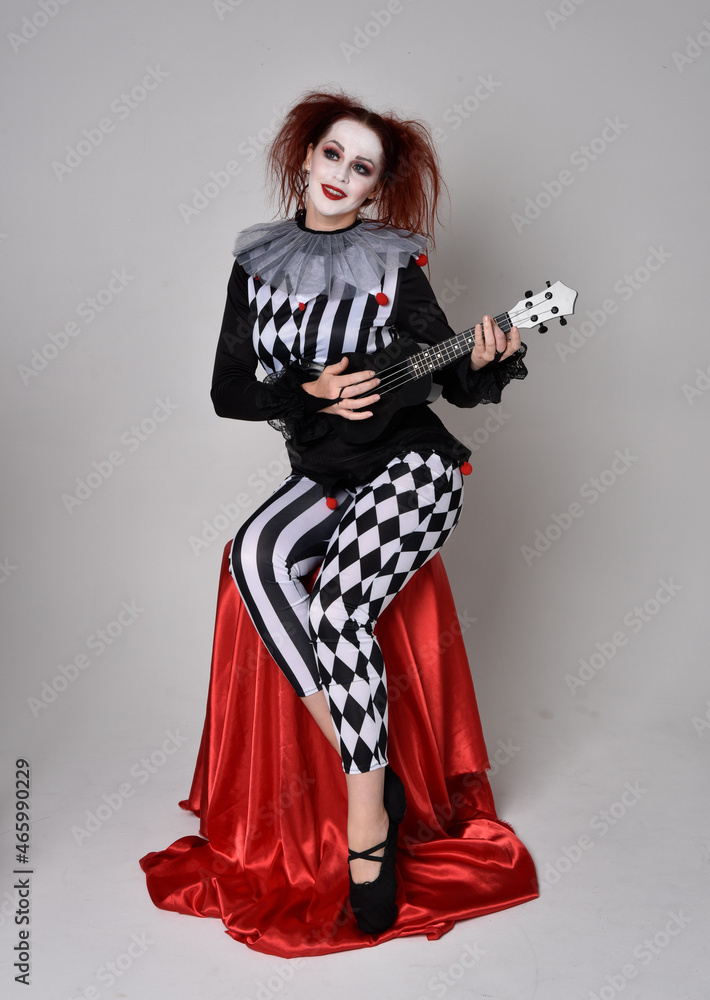Full length portrait of red haired girl wearing a black and white clown ...