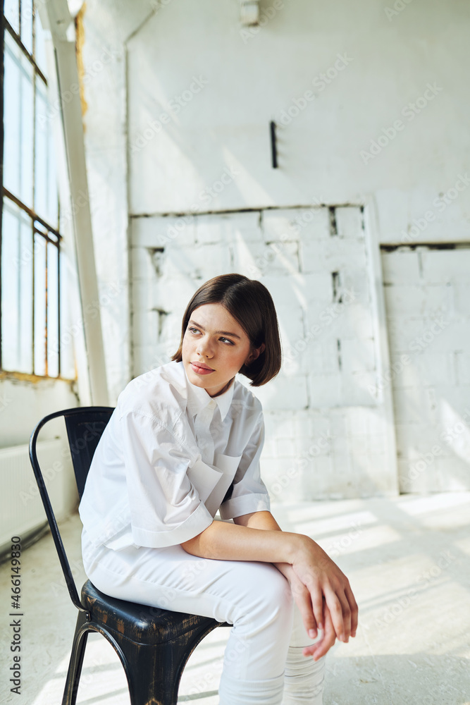 Beautiful teenager girl sitting on black stool in white shirt and pants ...