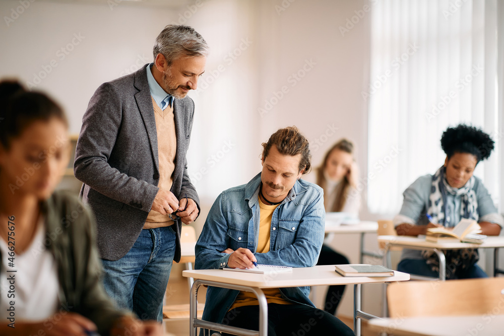 Smiling mature professor assists his student with lecture during class ...