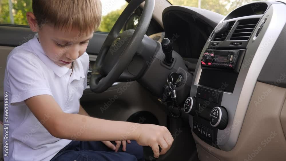 A little boy in a white T-shirt sits behind the wheel in a car and ...