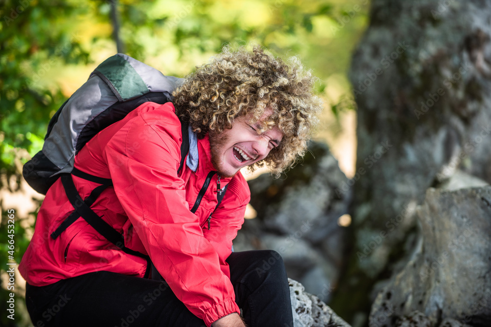Afro teenager injured during hiking sitting on a rock holding his leg ...