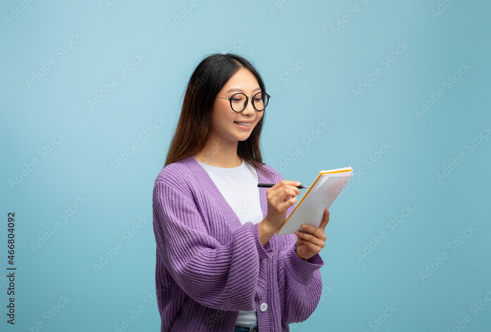 Intelligent asian lady in glasses taking notes, holding notepad and pen ...