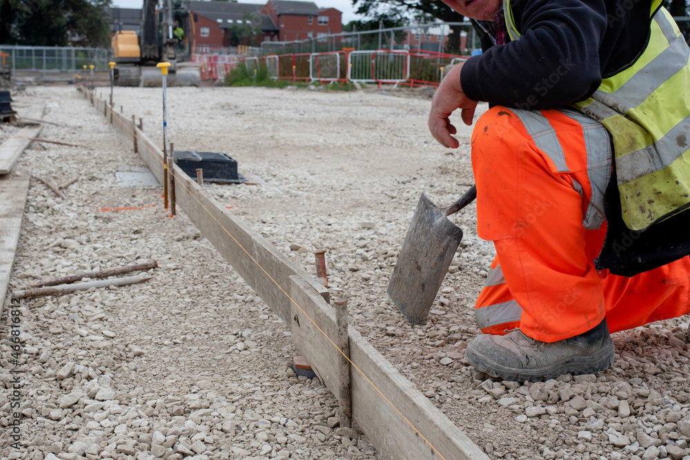 Groundworker in orange safety hi vis trousers fixing a timber along ...
