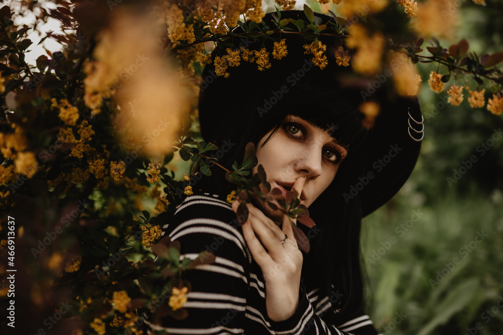 A girl in a black hat and a striped blouse poses in barberry flowers ...