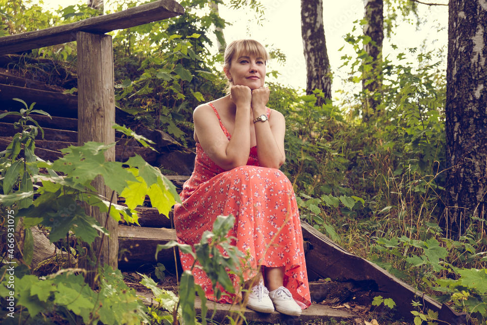 A young beautiful blonde woman of Slavic appearance sits on a wooden ...