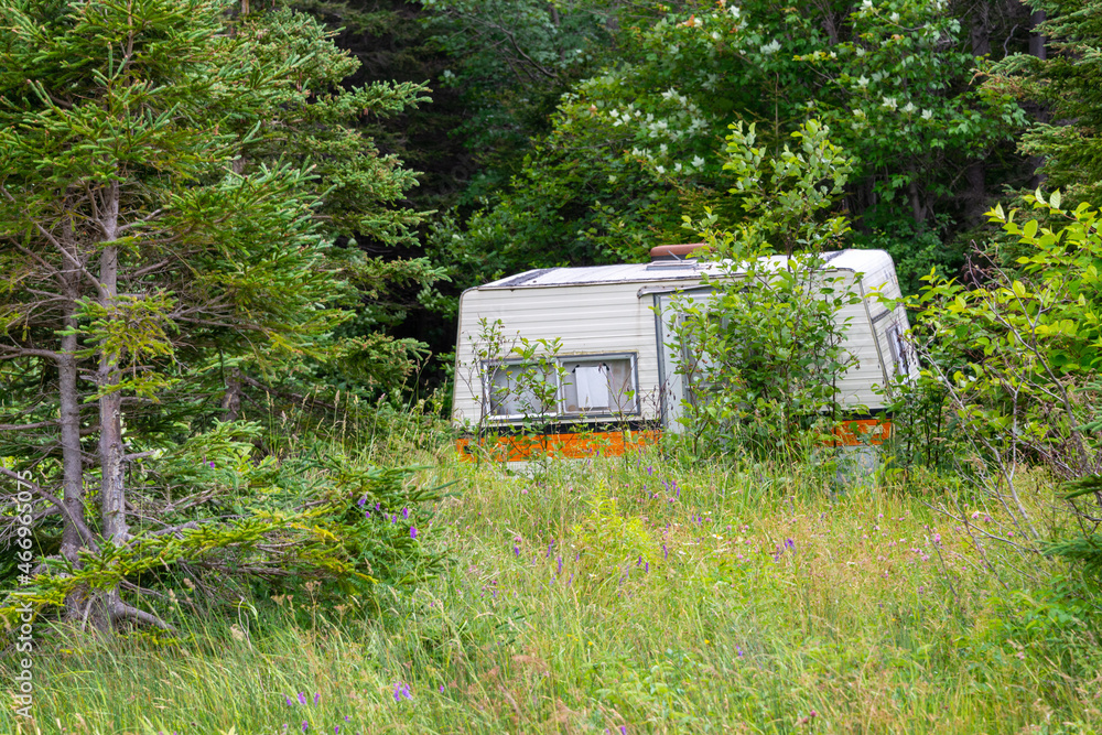 An abandoned travel trailer, white and orange in color, deserted in a ...