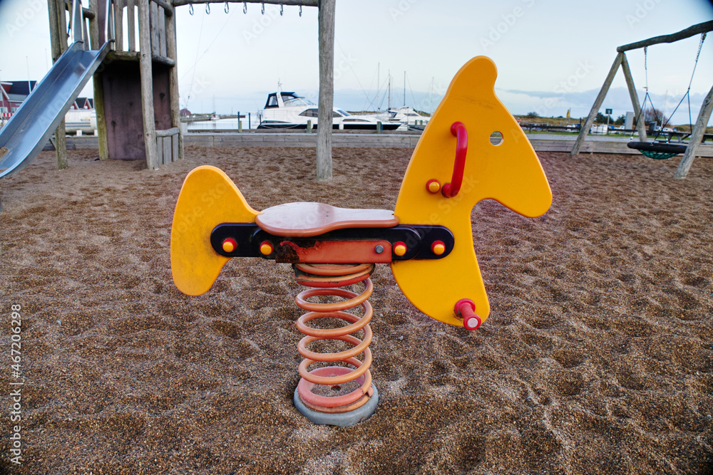 Spring horse toy on children's playground beside the harbor. Yellow or ...
