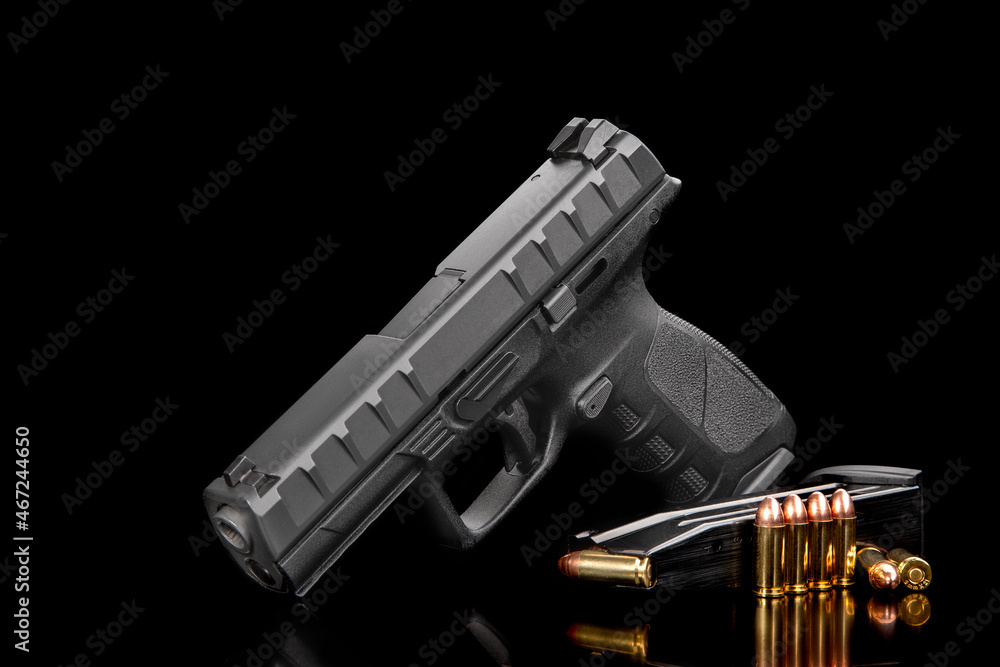 Black modern gun and ammunition for it on a dark reflective surface ...