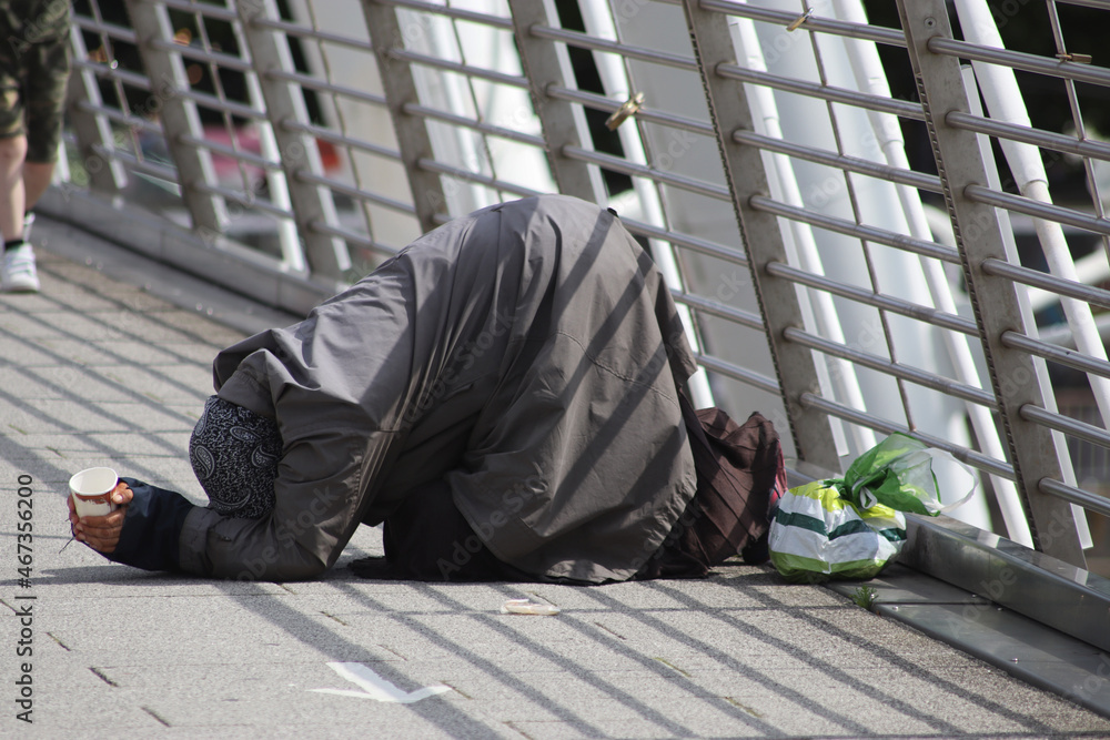 Person bending on the ground with the head down and asking for alms ...