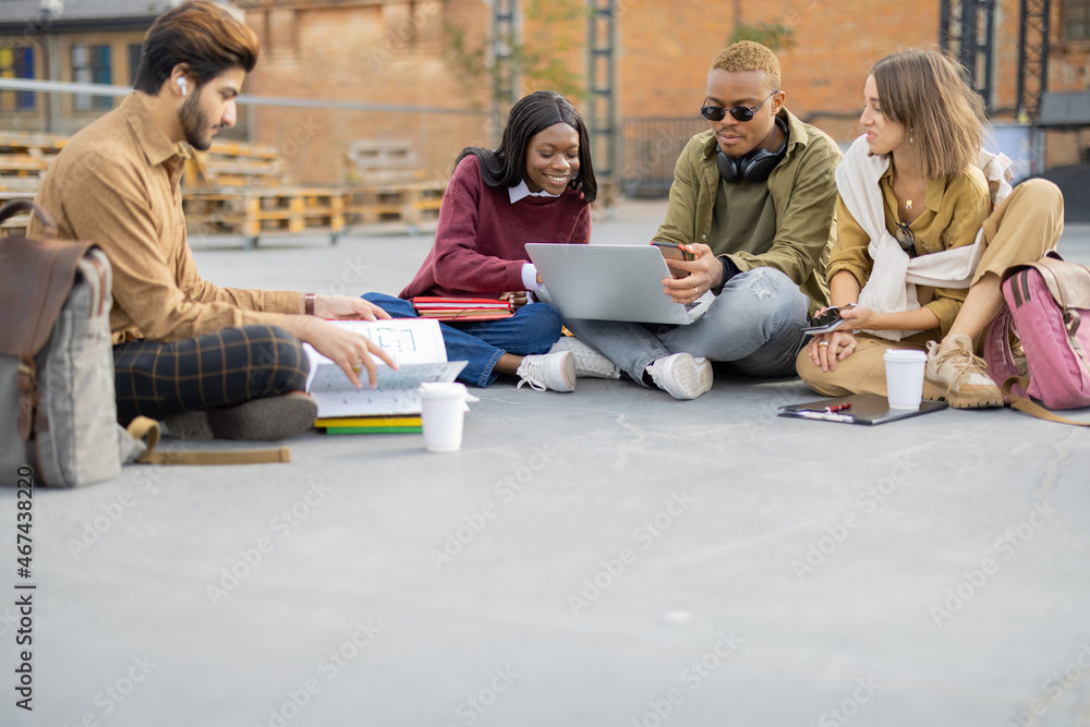 Multiracial students sit and learn on asphalt at university campus ...