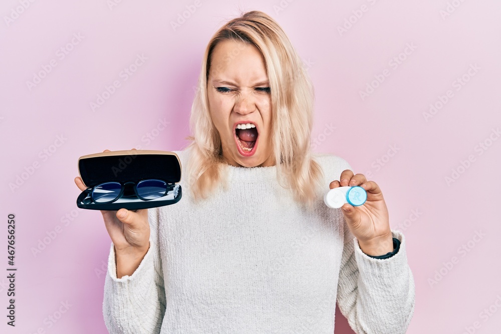 Beautiful caucasian blonde woman holding glasses and contact lenses ...
