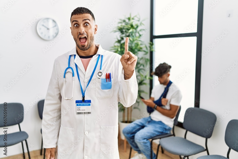 Hispanic doctor man at waiting room with pacient with arm injury ...