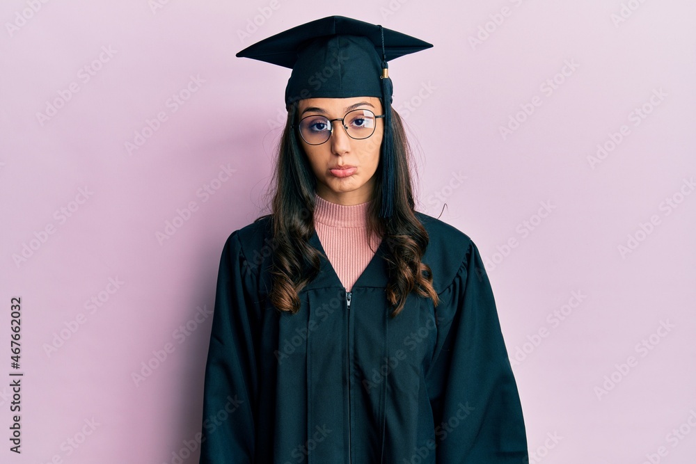 Young hispanic woman wearing graduation cap and ceremony robe depressed ...