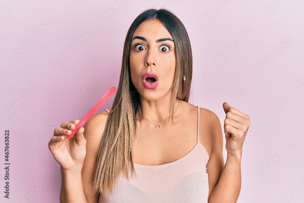 Young hispanic woman using file nail scared and amazed with open mouth ...