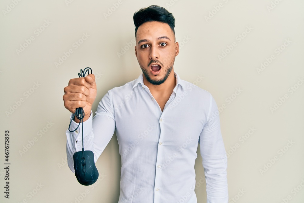 Young arab man holding computer mouse device scared and amazed with ...