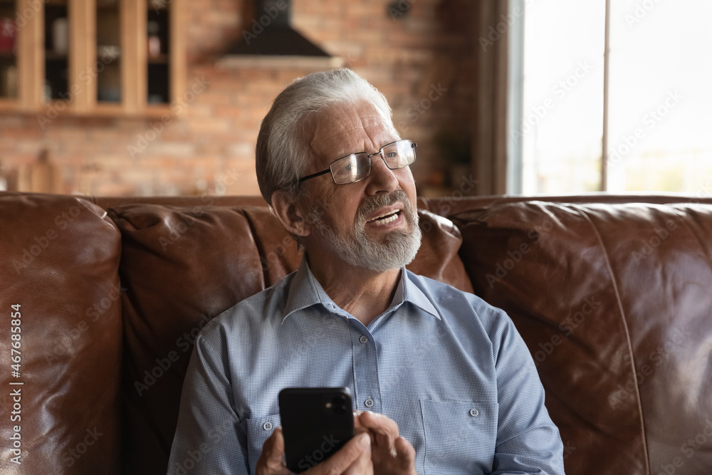 Thoughtful old age man sit on couch hold phone look aside distracted ...
