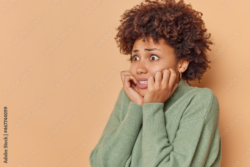 Terrified scared young woman looks terrified at something bitess finger ...