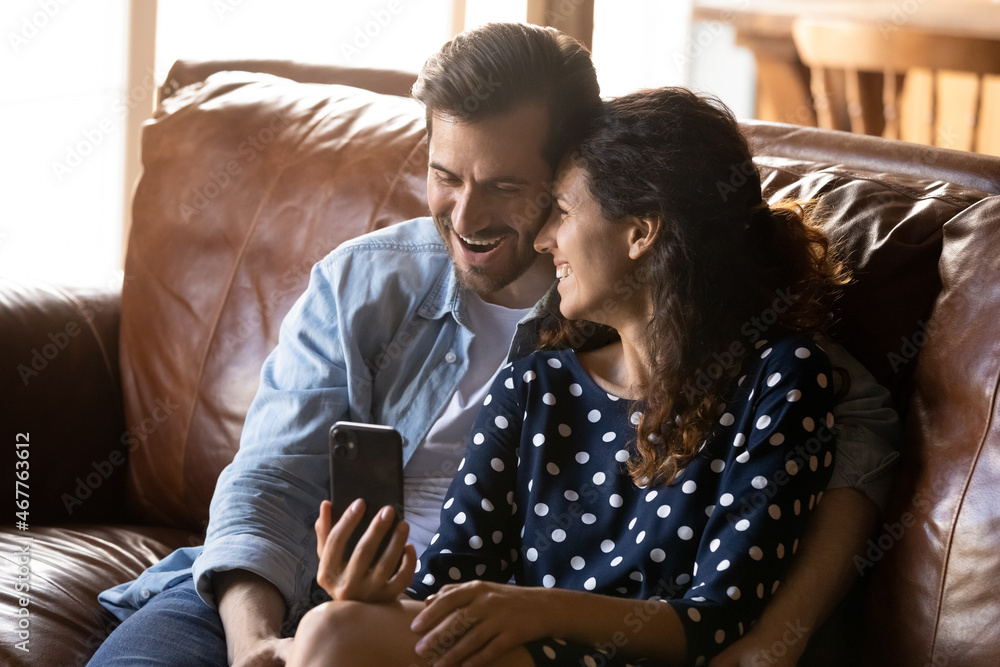 Funny thing. Overjoyed young married couple cuddle on sofa watch cute ...