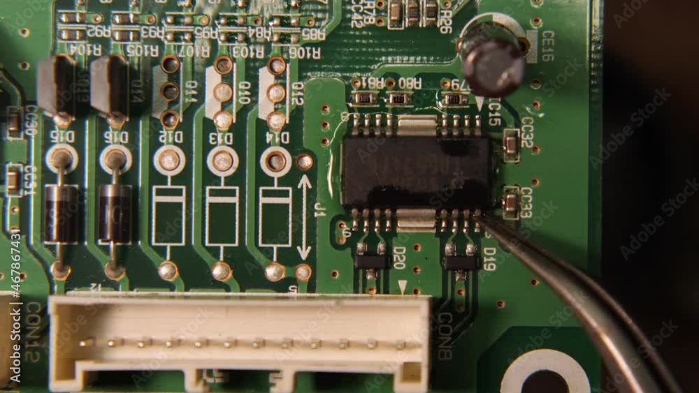 The repairman uses tweezers to remove a chip from the board underneath ...