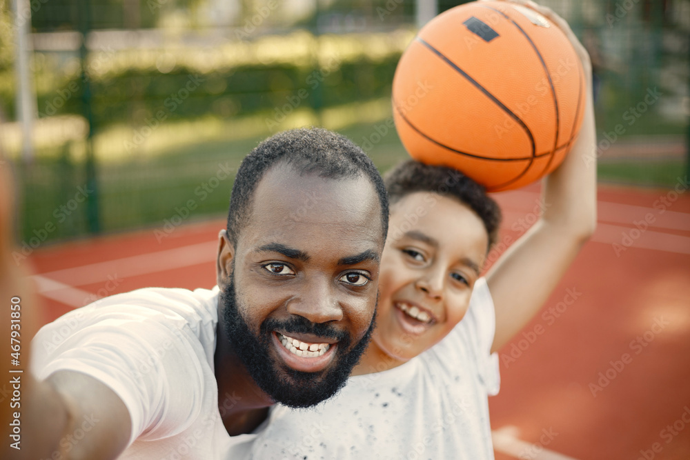 Black father with his multiracial son standing on a basketball court ...