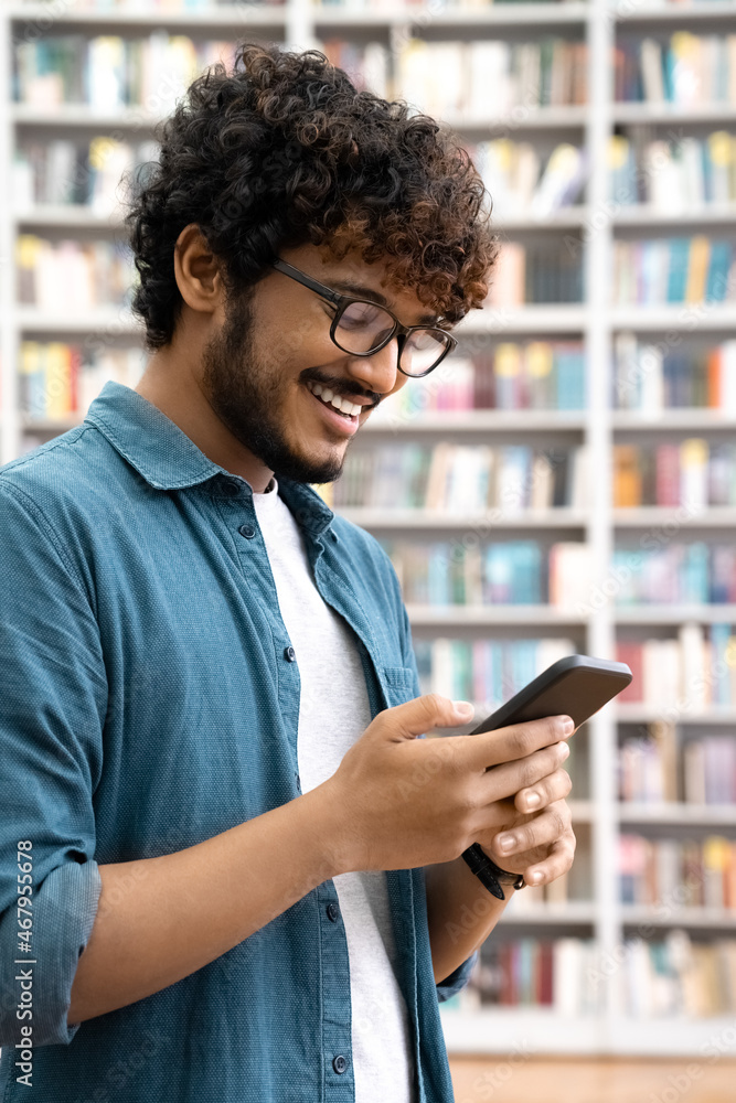 Side view on smart young Indian student using mobile phone in library ...