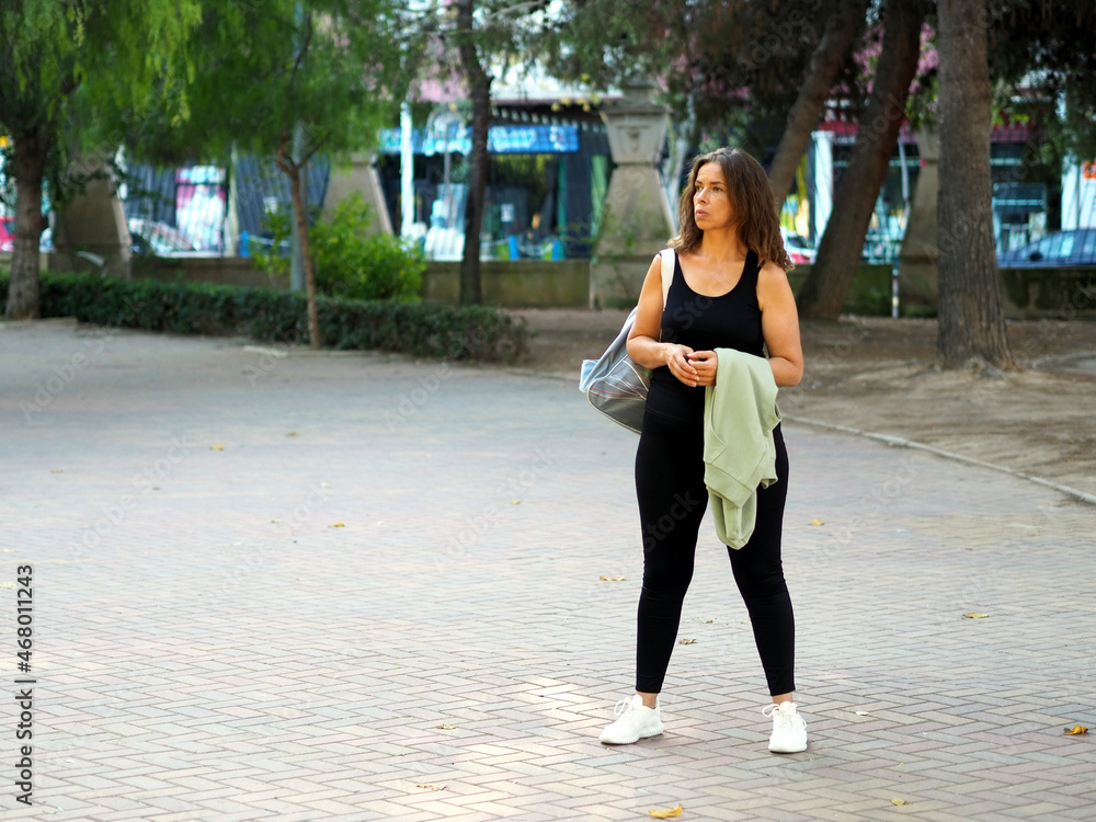 A 45+ year old woman in sportswear and a gym bag in the park. Sports ...
