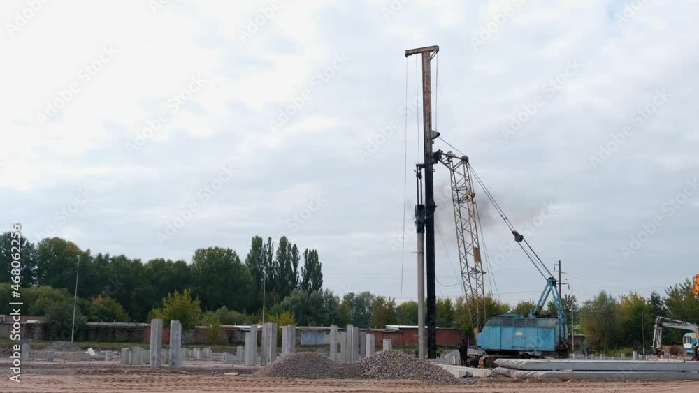 A large vertical piling crane equipped with a diesel hammer hammers ...