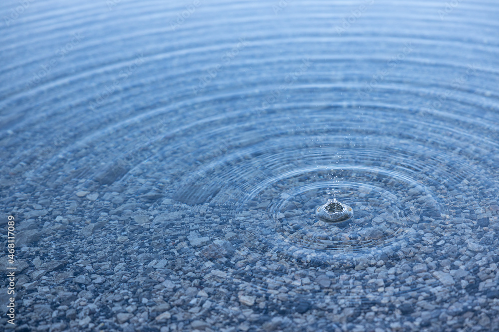 Wassertropfen erzeugen Wellen in einem See mit Steinen am Grund. Das ...