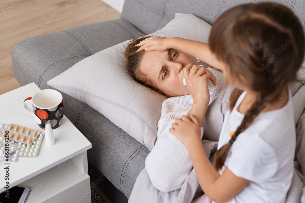 Little girl sitting on sofa near sick mother, ill female having a high ...