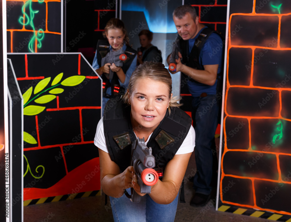 Positive young woman with laser gun during lasertag game with players ...