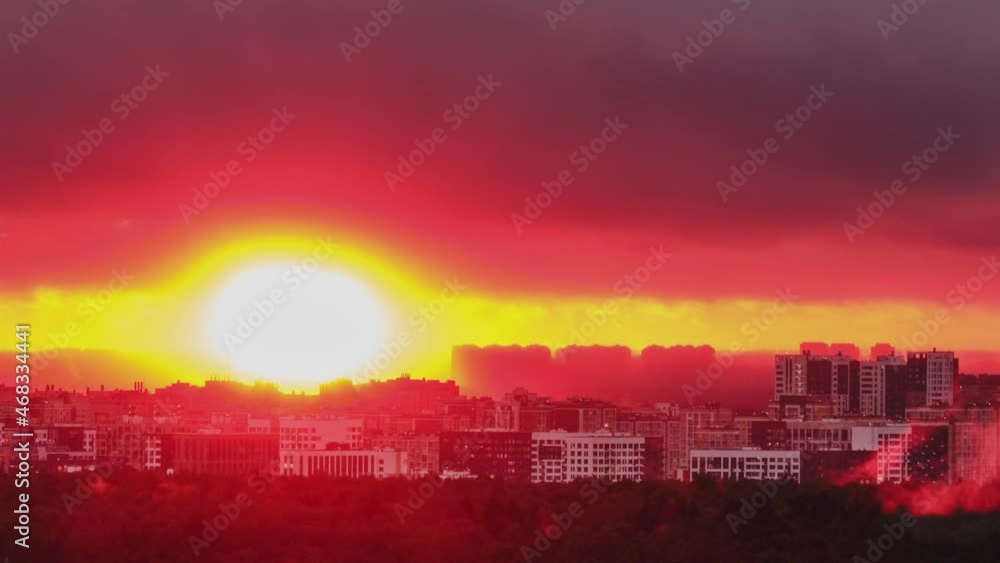Big red sun in dark clouds behind silhouettes of city houses, time ...