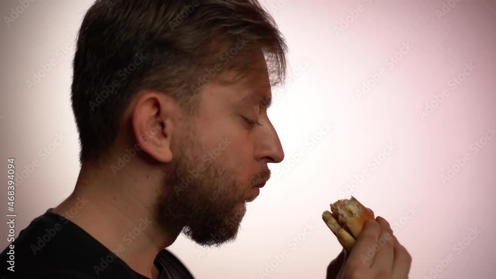 Shot in profile of young man eating with pleasure hamburger, hungry ...