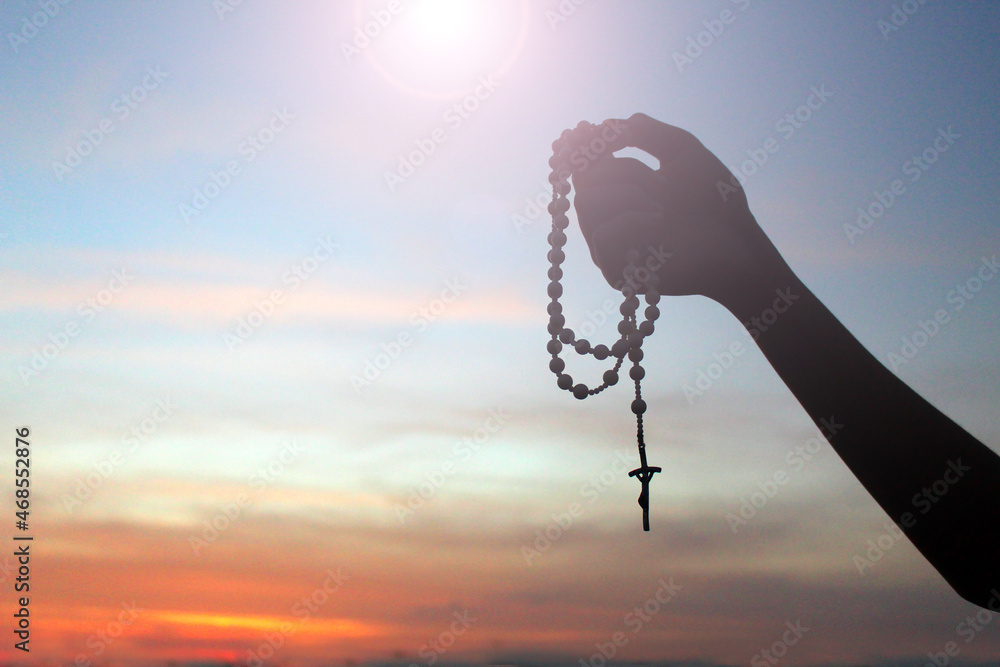 Silhouette of a hand holding Rosary on colorful sunset sky light ...