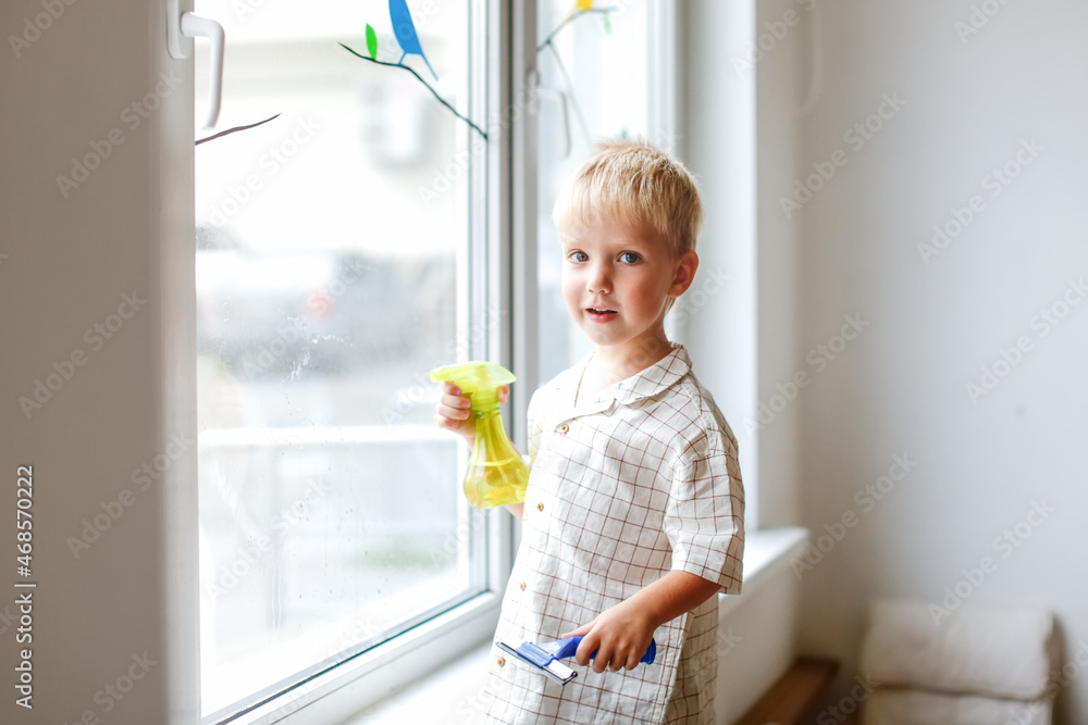 Cute boy toddler blond toddler at the window washes the glass. Helping ...