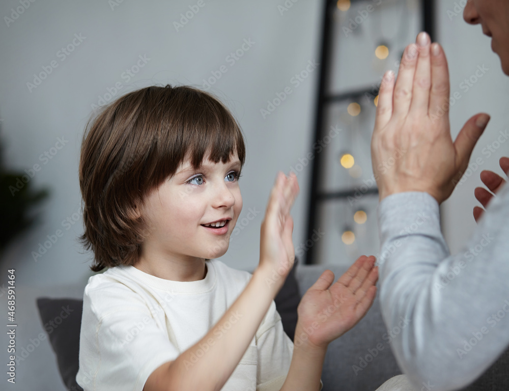 Smiling male kid rejoicing hitting palm clapping hands to woman nanny ...