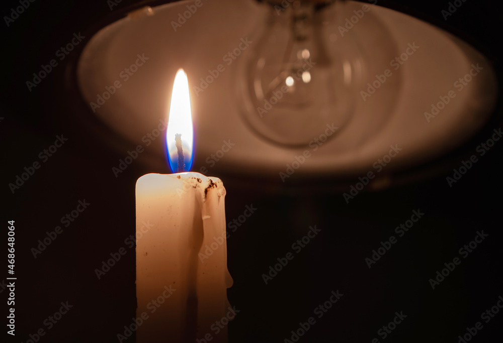 Burning candle near a switched off light bulb in complete darkness ...