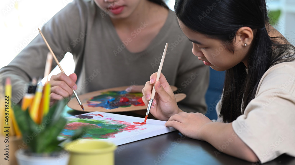 Young female teacher helping little girl painting picture in art class ...