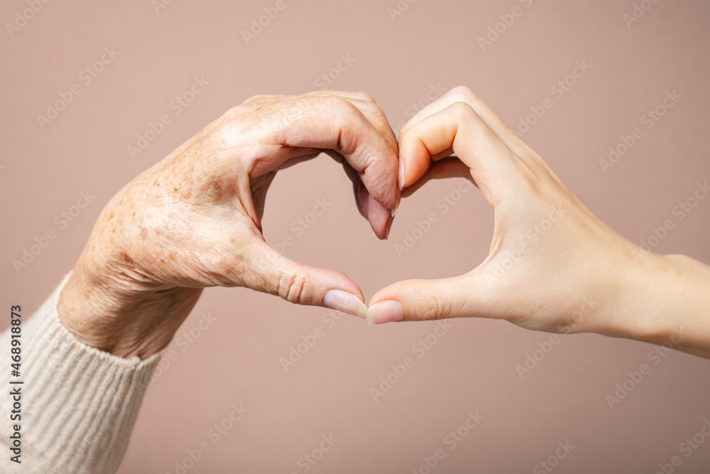 Hands of a young and senior woman make a heart gesture. Close up. Beige ...