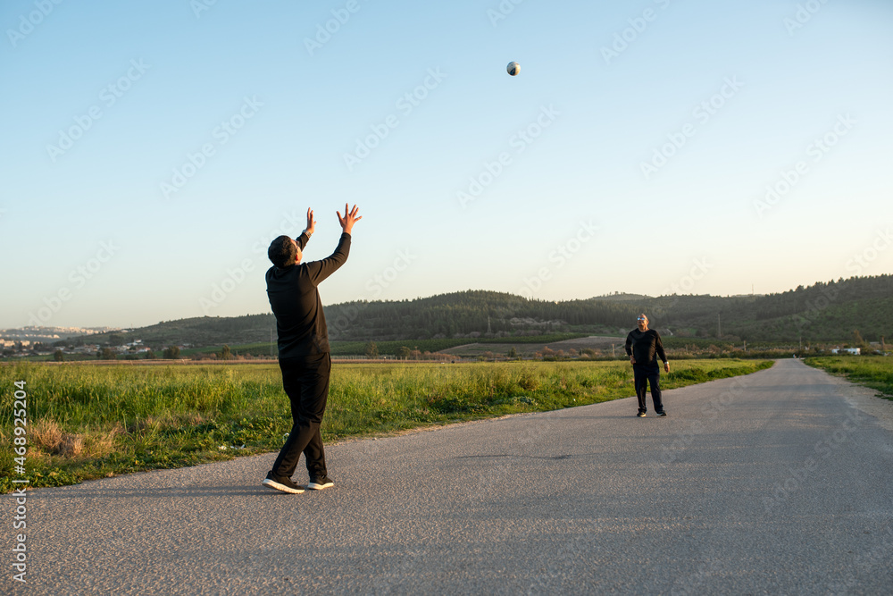 Elderly father throwing ball into the air and teen son preparing to ...