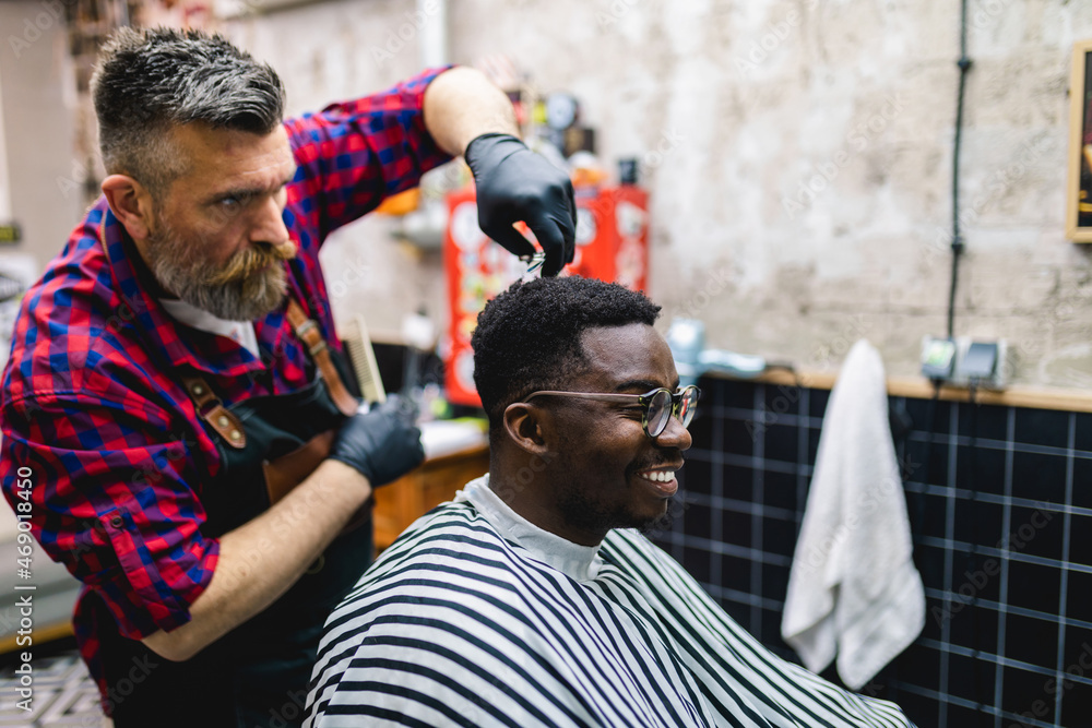 Young African man visiting hairstylist in barber shop. Professional ...